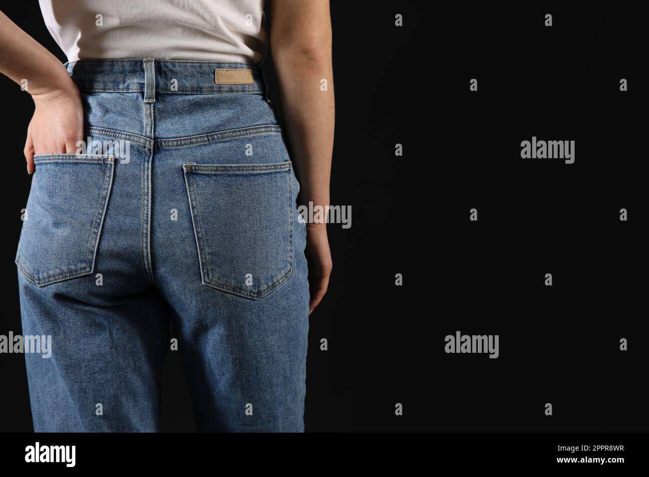 Young woman in stylish jeans on black background, back view Stock Photo ...