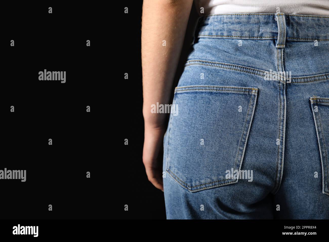 Young woman in stylish jeans on black background, back view Stock Photo ...