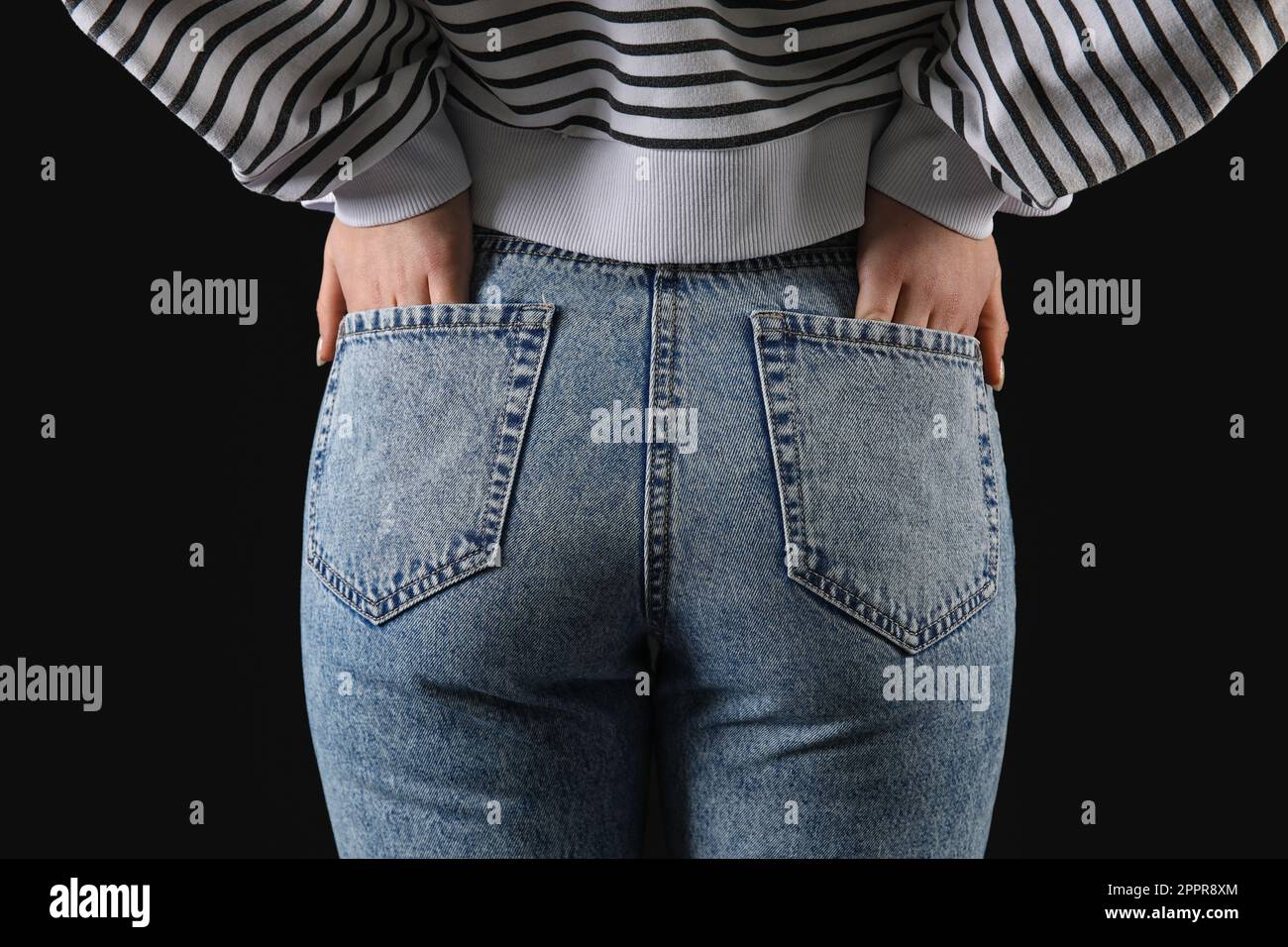 Young woman in stylish jeans on black background, back view Stock Photo ...