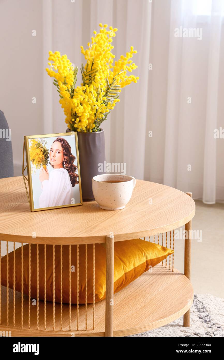 Coffee table with flower vase, cup and photo of woman in interior of ...