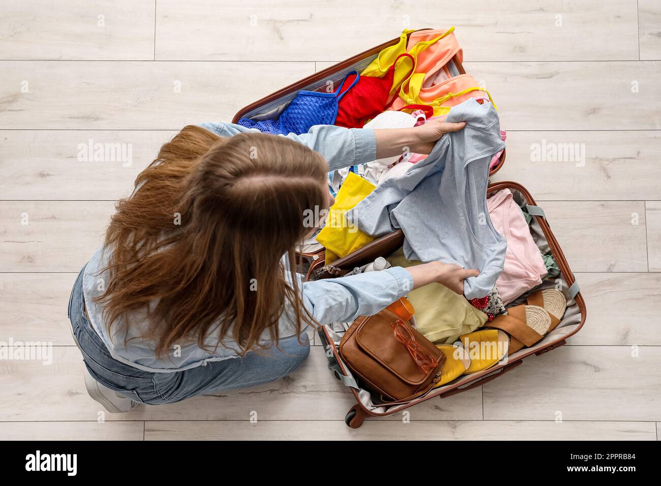 Young woman unpacking her clothes from suitcase on light wooden floor ...
