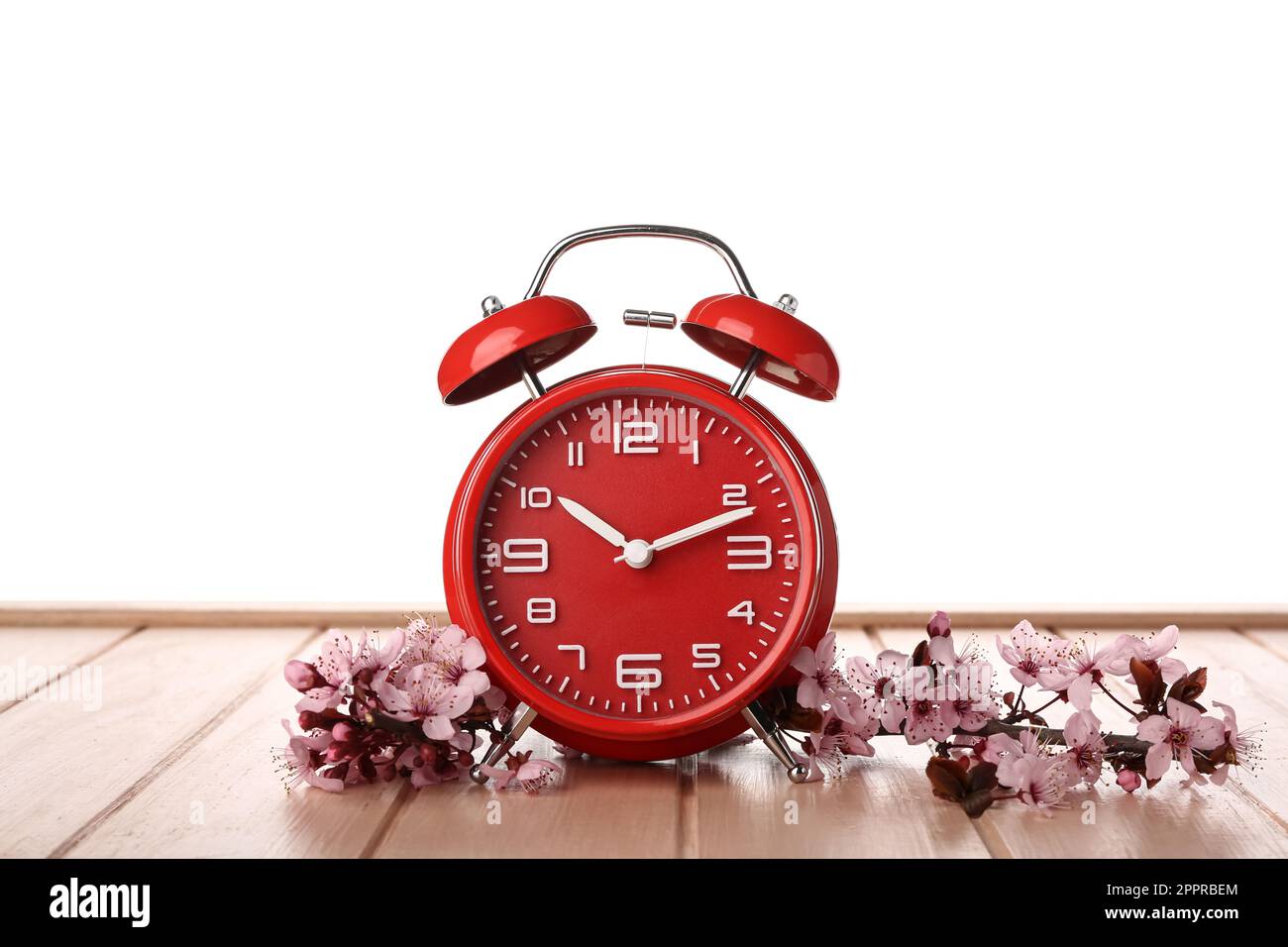 Blooming spring branches and alarm clock on table against white ...