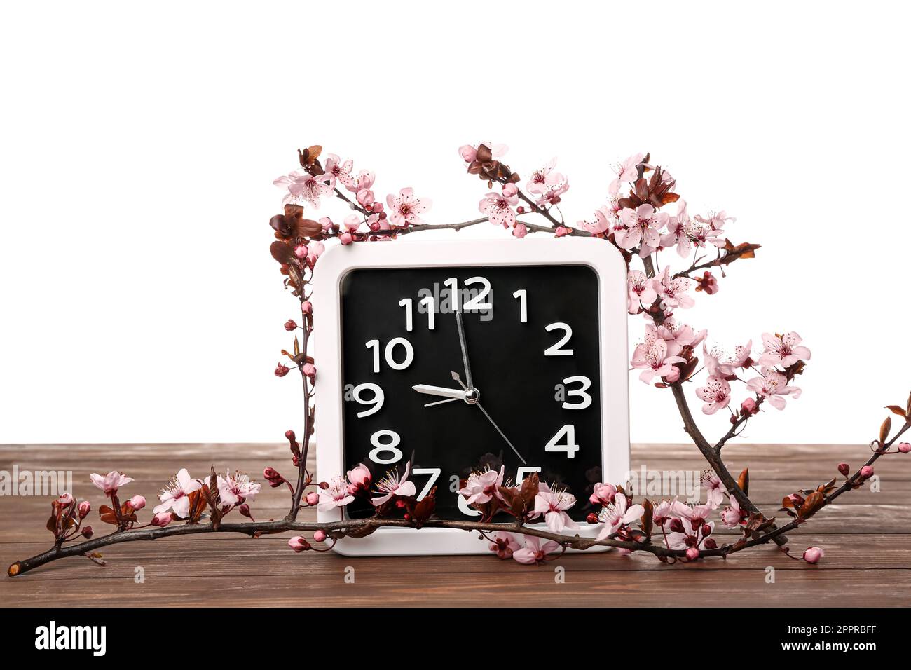 Blooming spring branches and clock on table against white background ...