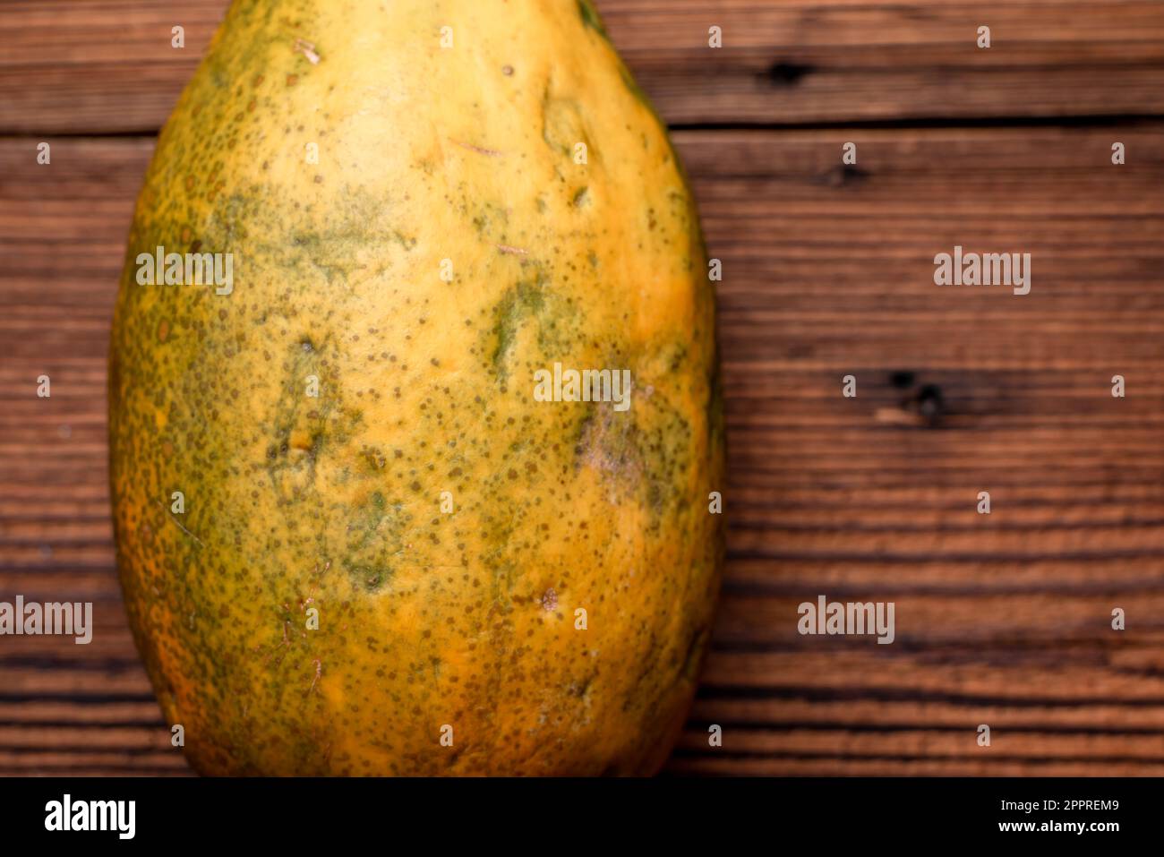 whole papaya on a wooden background. An imperfect-looking fruit with an ...