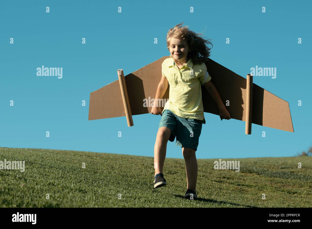Kid boy playing with cardboard wings. Child in summer field. Kids ...