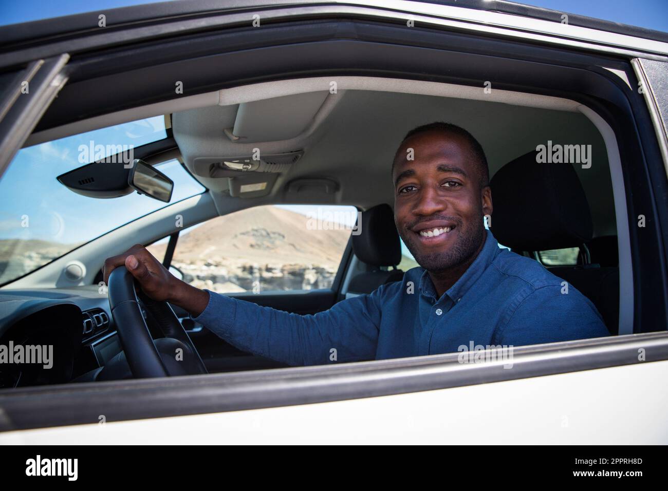A smiling African businessman sitting in his car as he is about to ...