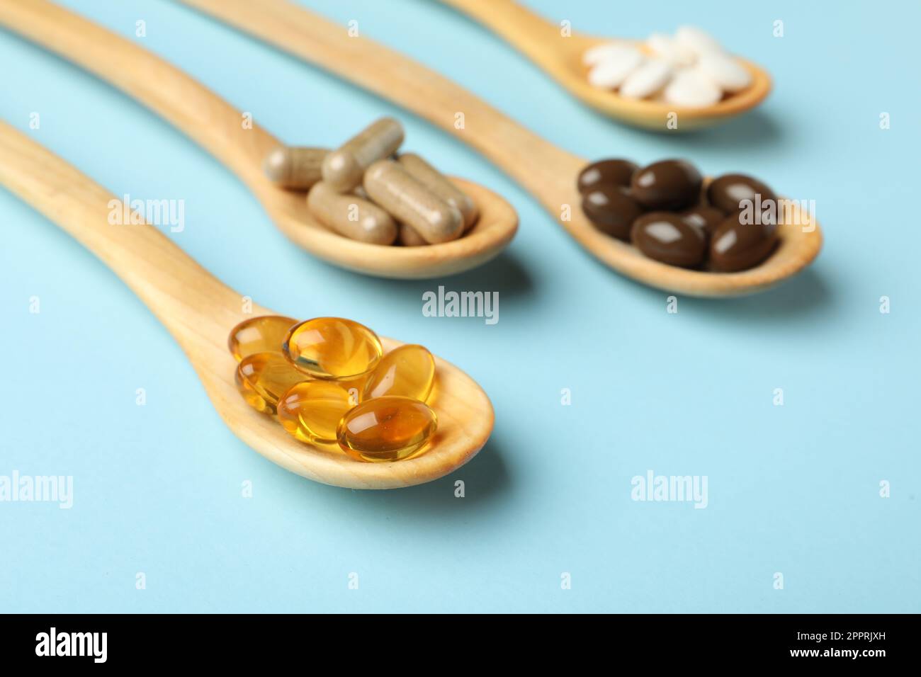 Wooden spoons with different dietary supplements on light blue ...