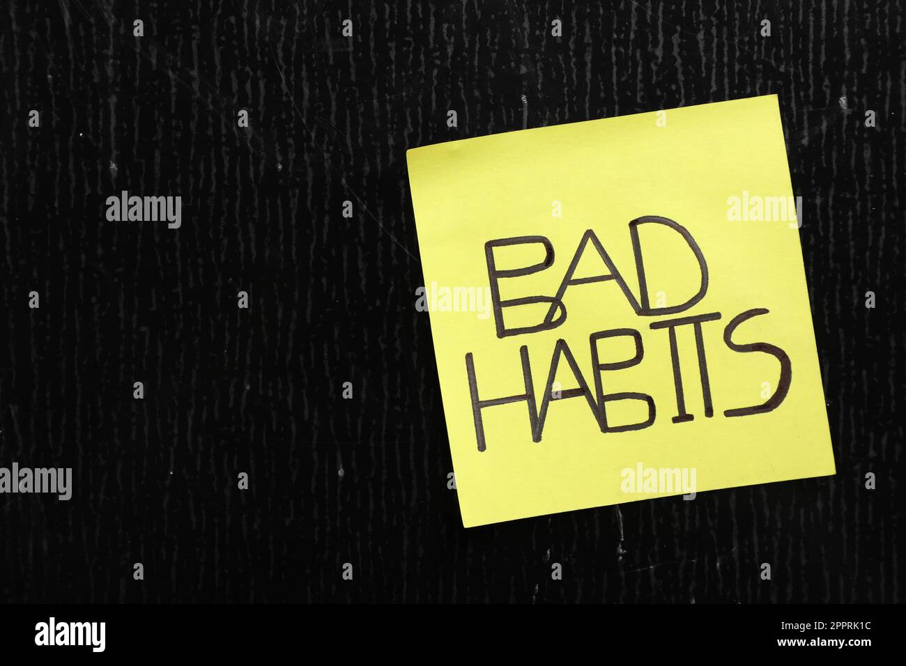 Paper note with phrase Bad habits on black board, closeup. Space for ...