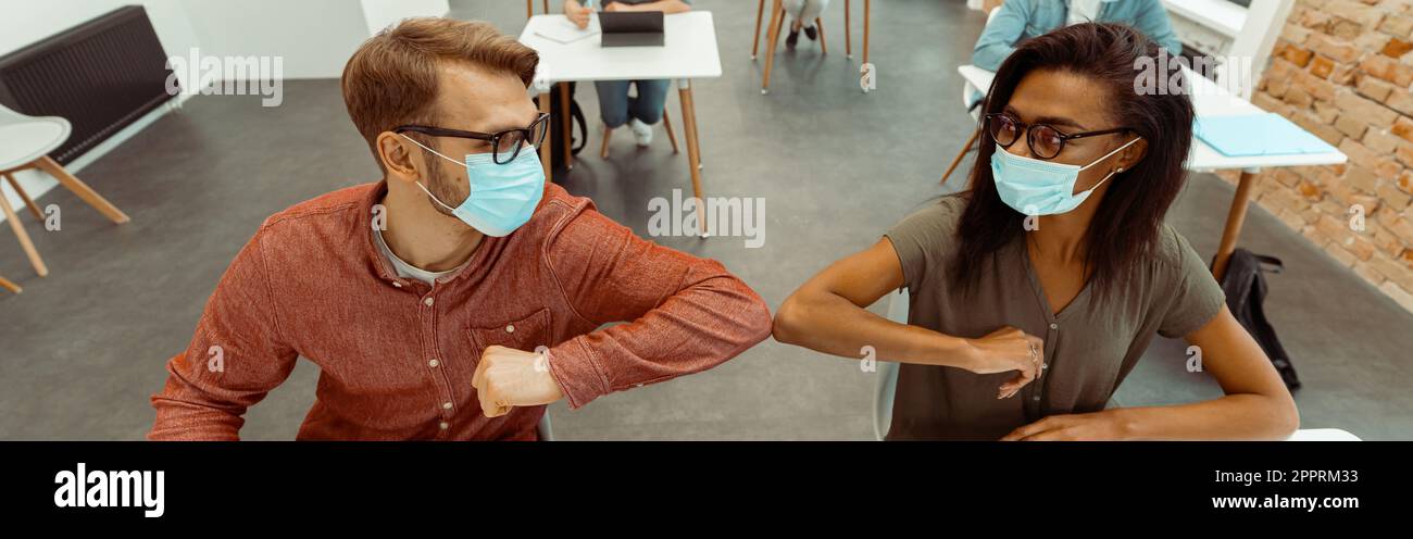 Two students greeting bumping elbows at workplace Stock Photo - Alamy