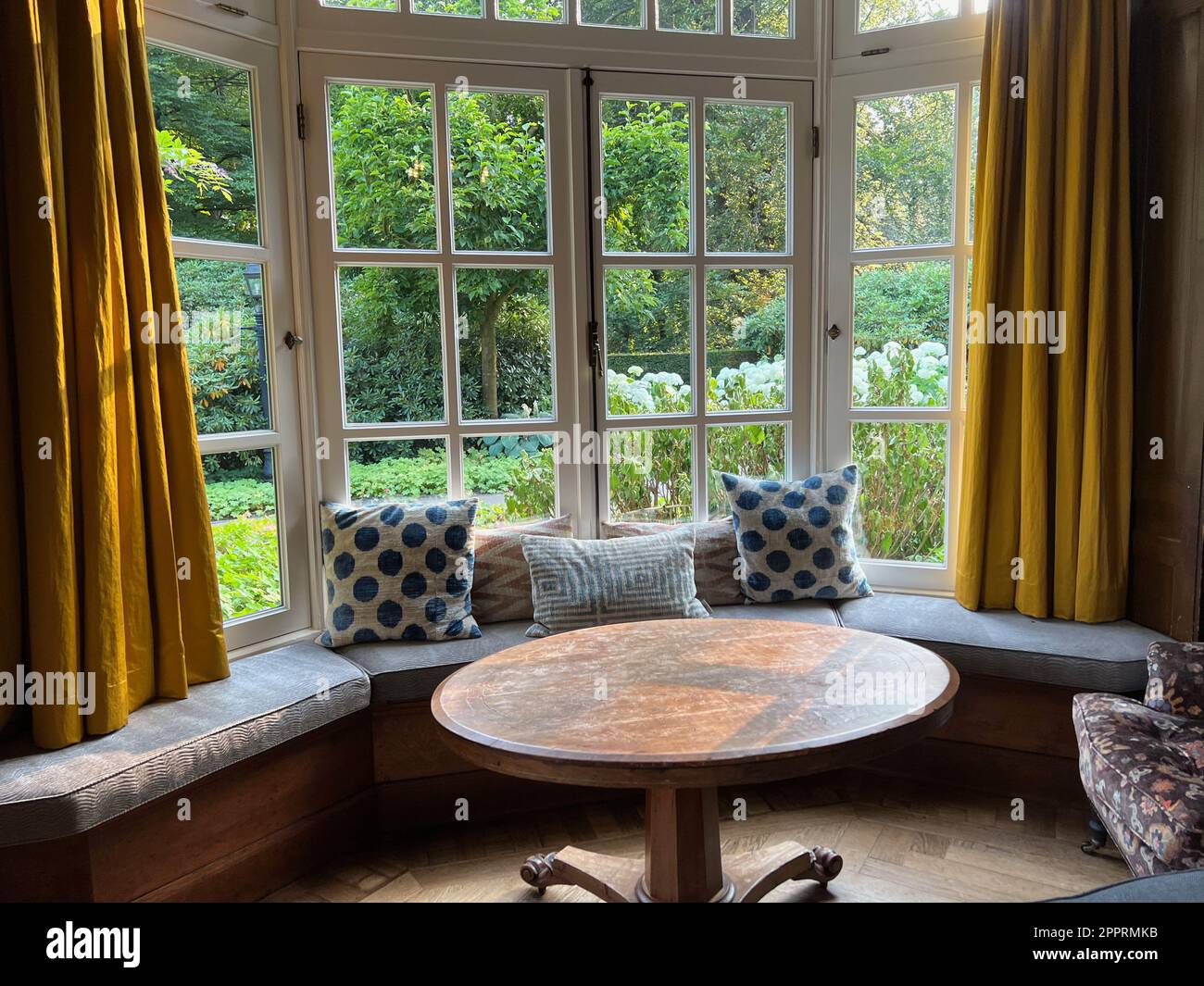 Wooden table near cozy bay window seat with cushions in room. Interior ...