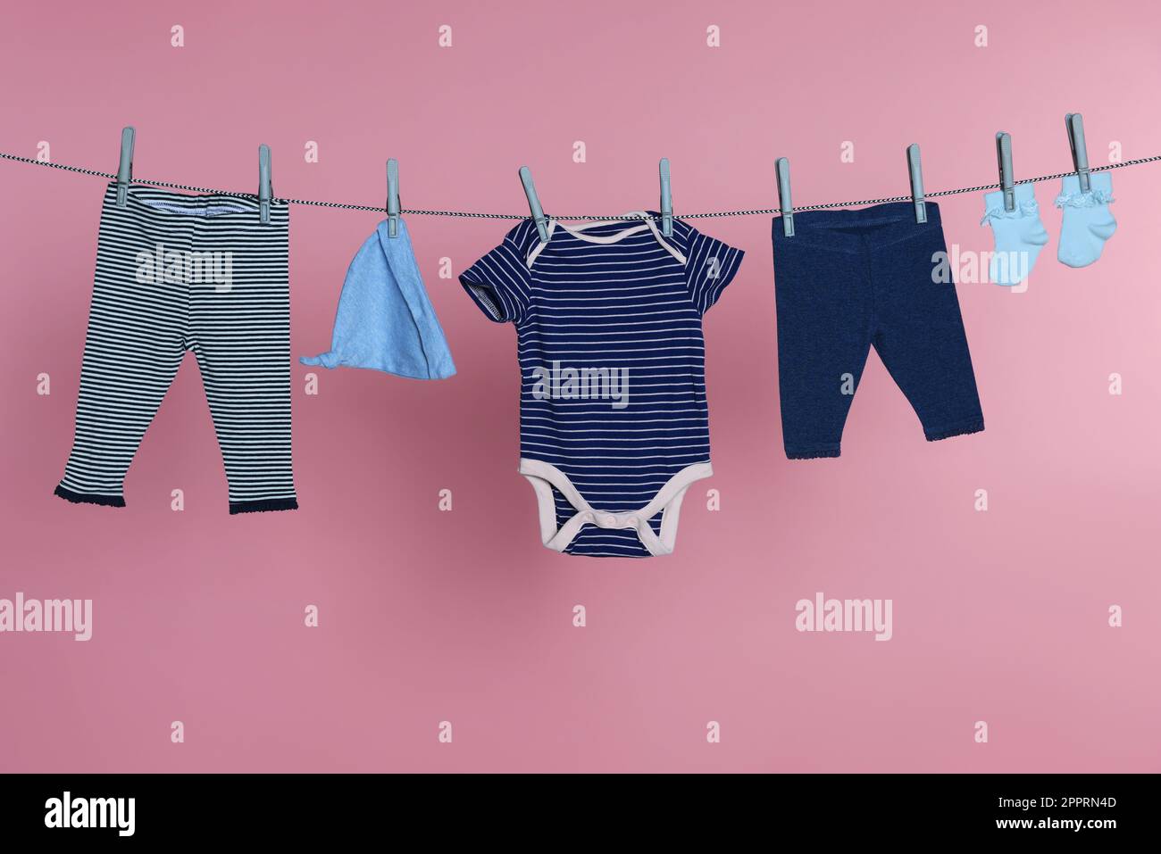 Different baby clothes drying on laundry line against pink background ...