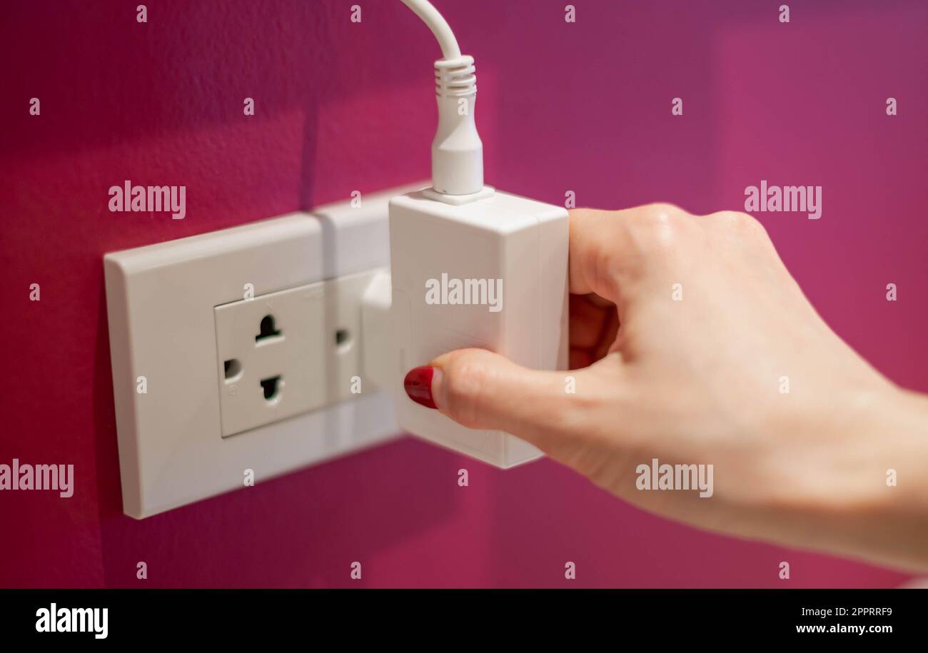 Hand is unplug the electric line off a white socket on the red wall ...