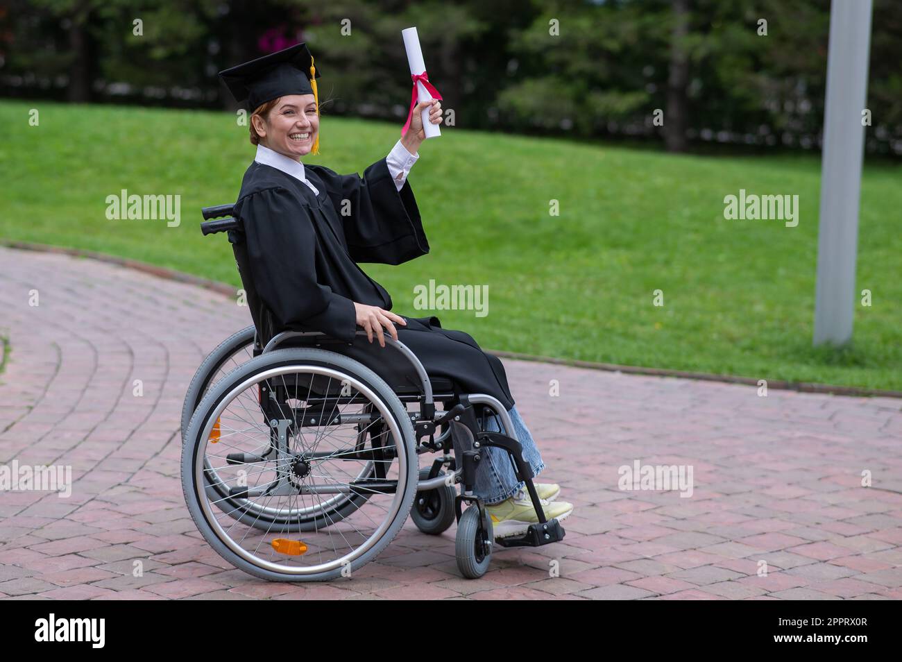 Caucasian woman in a wheelchair in a graduate costume rejoices at ...