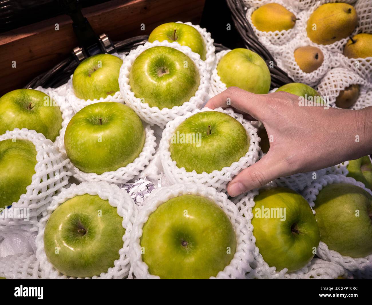 A female hand takes a green apple with packing foam net in super market ...