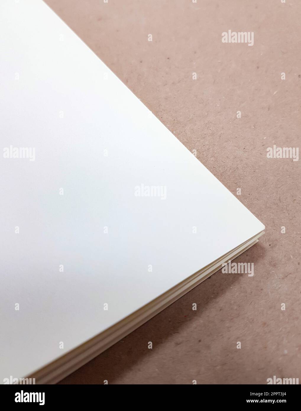 A corner of a stack of white paper sheets lies on a brown background ...