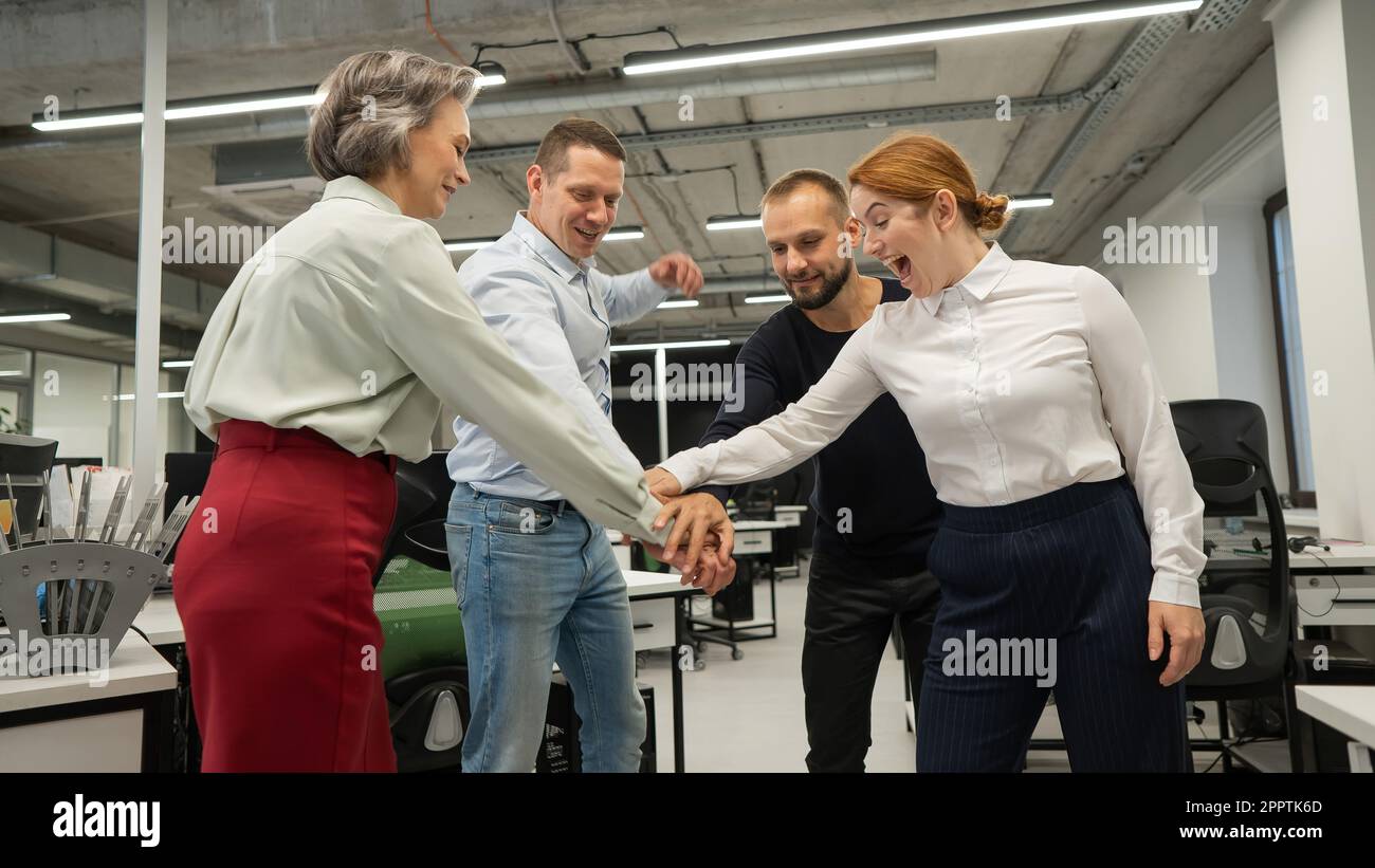 Four colleagues give the low five in the office Stock Photo - Alamy