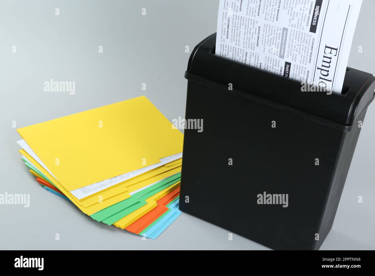 Shredder with sheet of paper and colorful folders on grey background ...