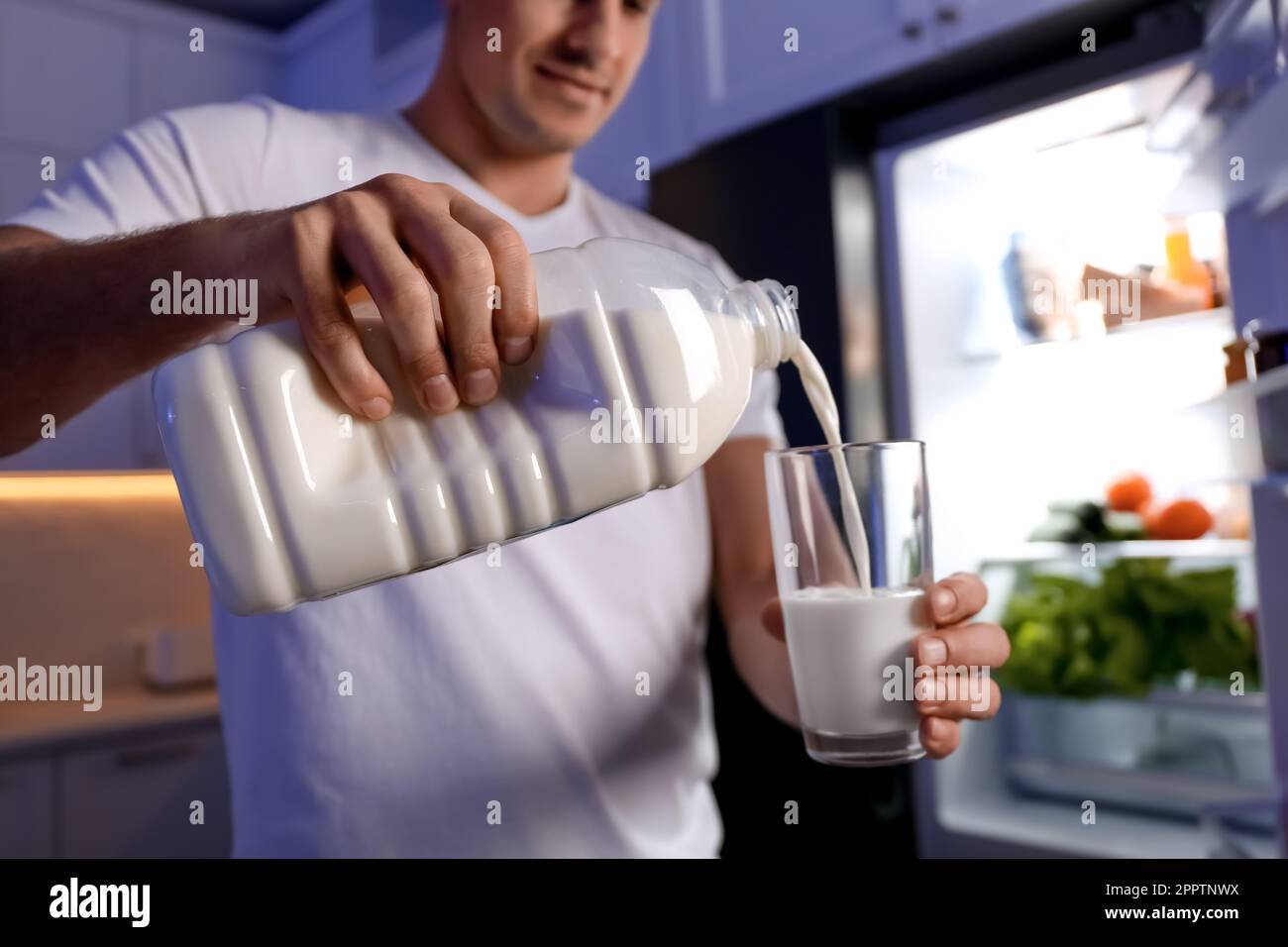 Man pouring milk from gallon bottle into glass near refrigerator in ...