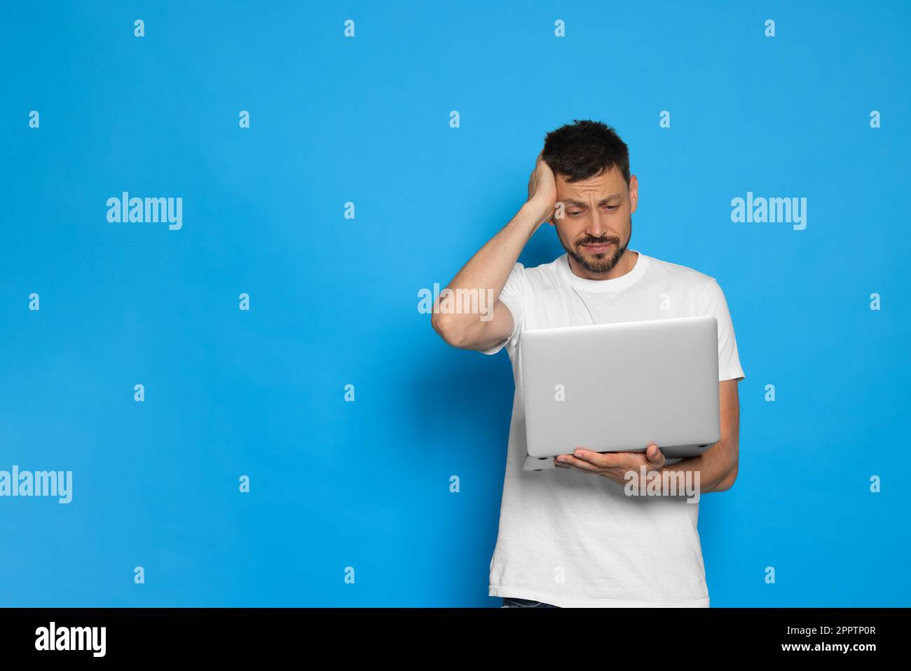 Confused man looking at laptop on light blue background. Space for text ...