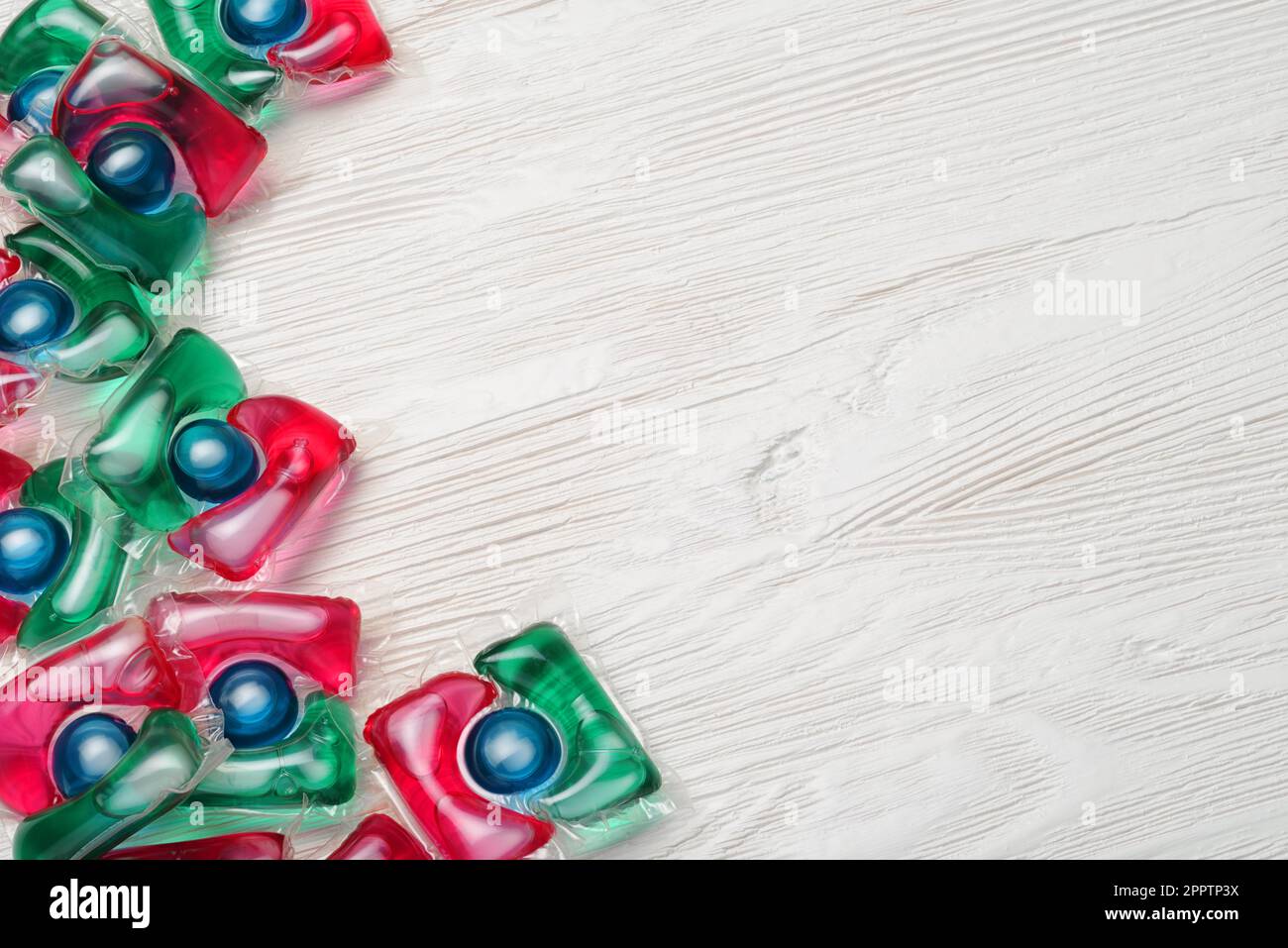 Pile of washing gel capsule pods with laundry detergent on white wooden ...