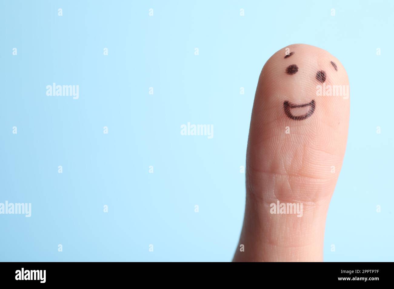 Finger with drawing of happy face on light blue background. Space for ...
