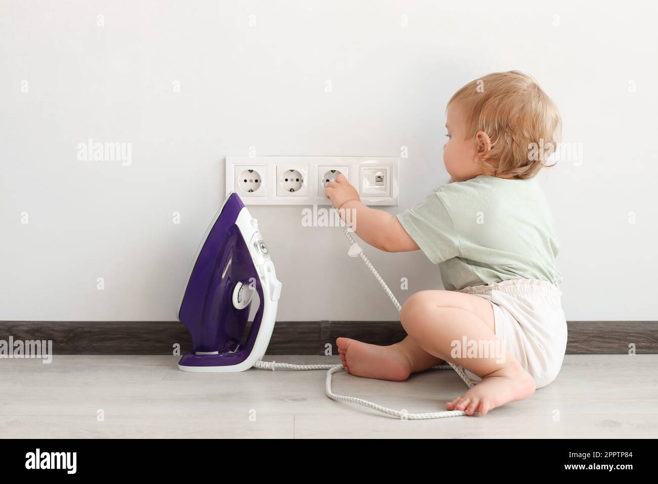 Cute baby playing with electrical socket and iron plug at home ...