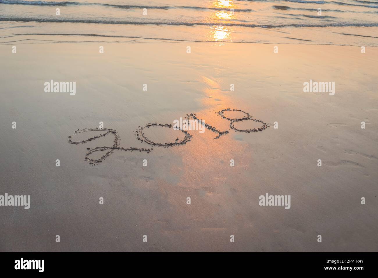 Numbers 2018 handwritten on sand at the beach during sunset time ...