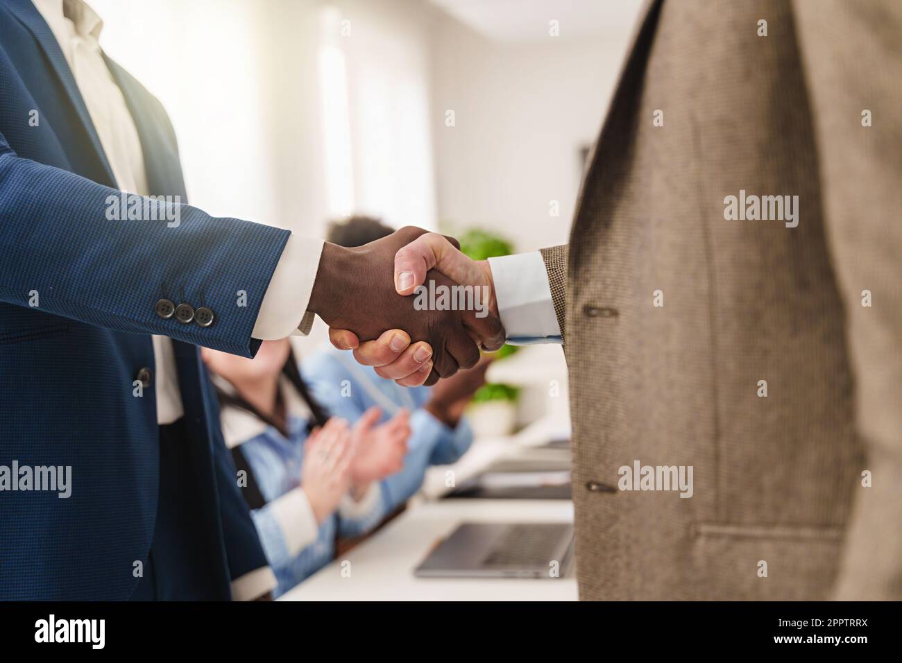 Close-up of two businessmen shaking hands in an office setting with ...