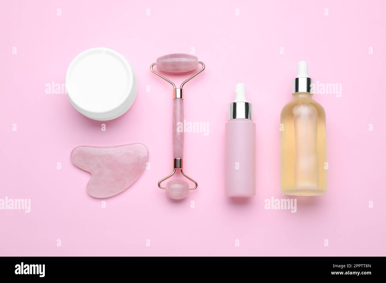 Natural face roller, gua sha tool and cosmetic products on pink ...