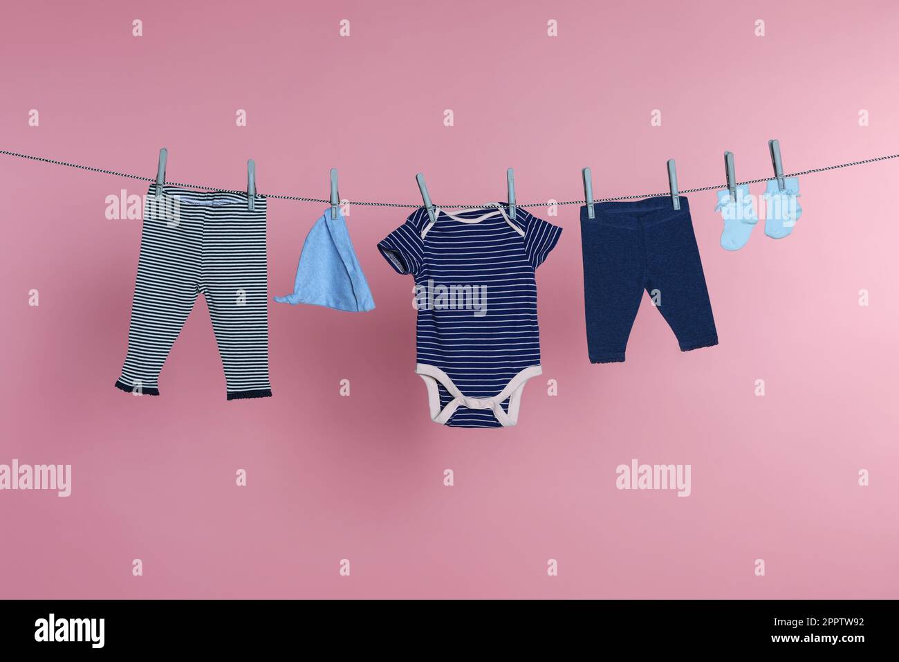 Different baby clothes drying on laundry line against pink background ...