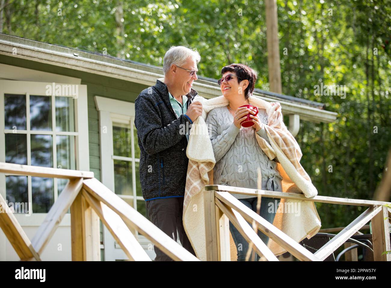 Mature couple standing on porch and drinking hot coffee from mug. They ...