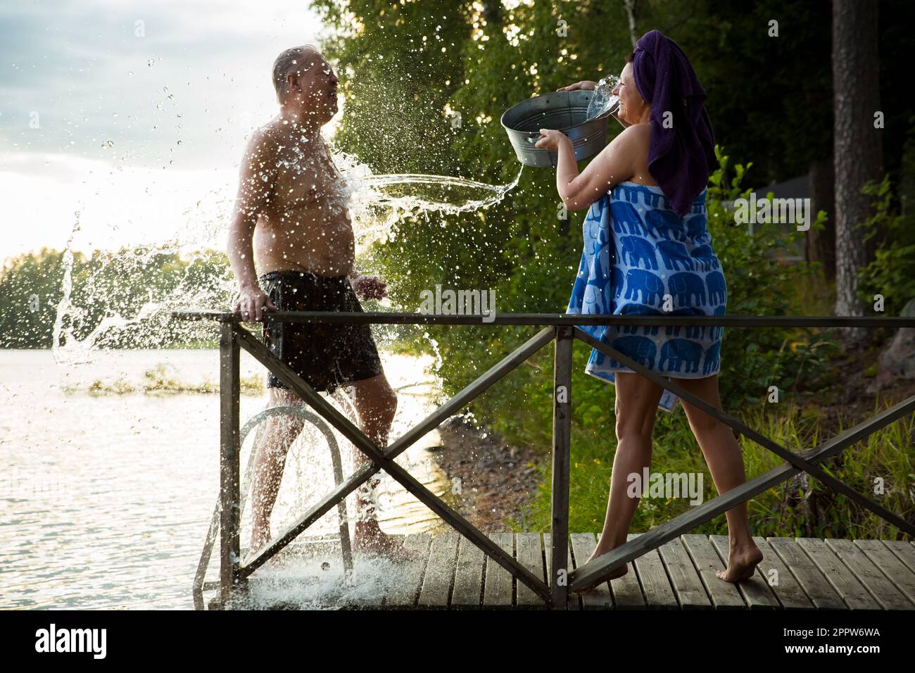 Aged couple having fun after Finnish sauna on wooden cottage pier in a ...