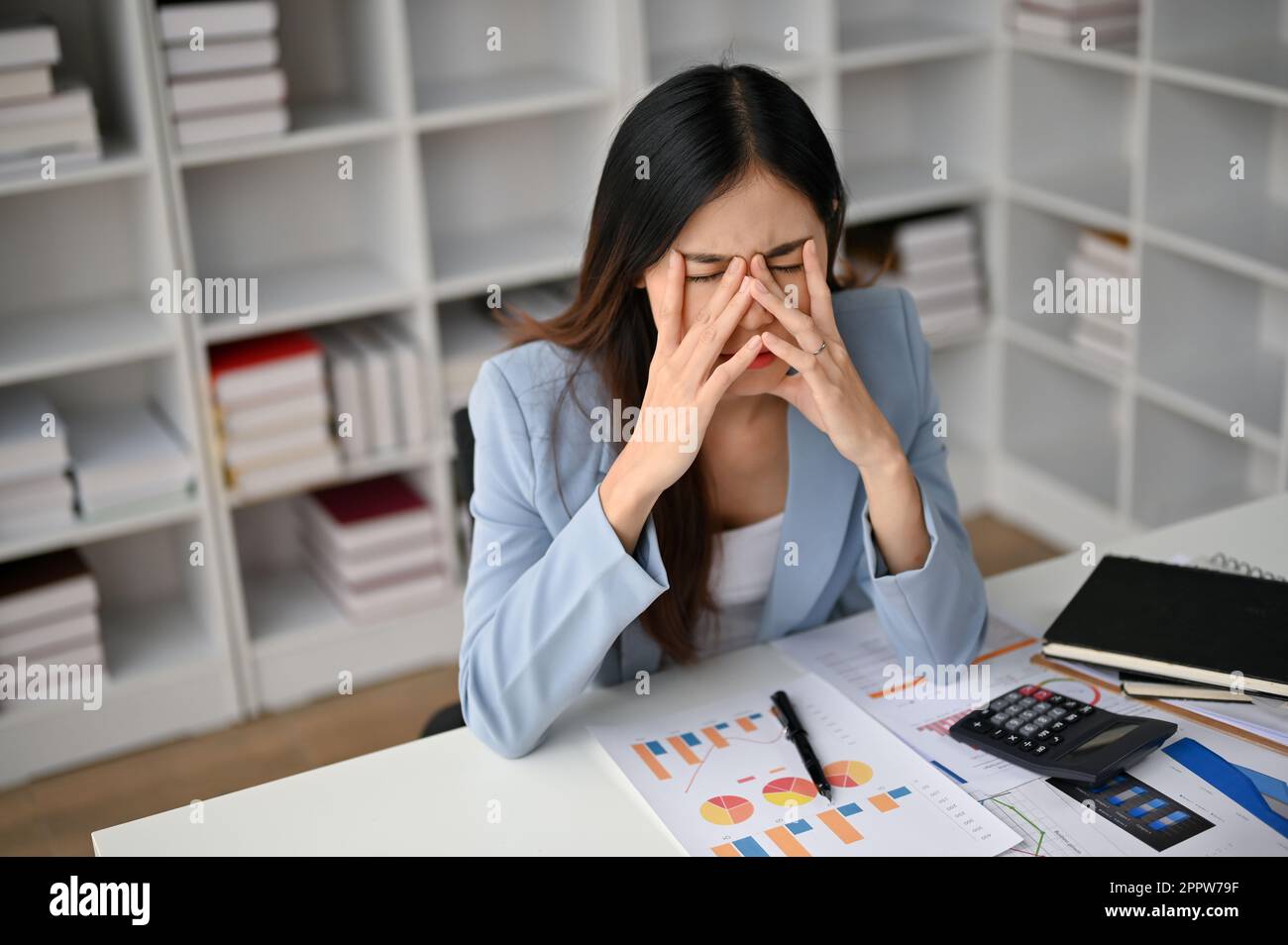 Tired and stressed millennial Asian businesswoman sits at her desk ...