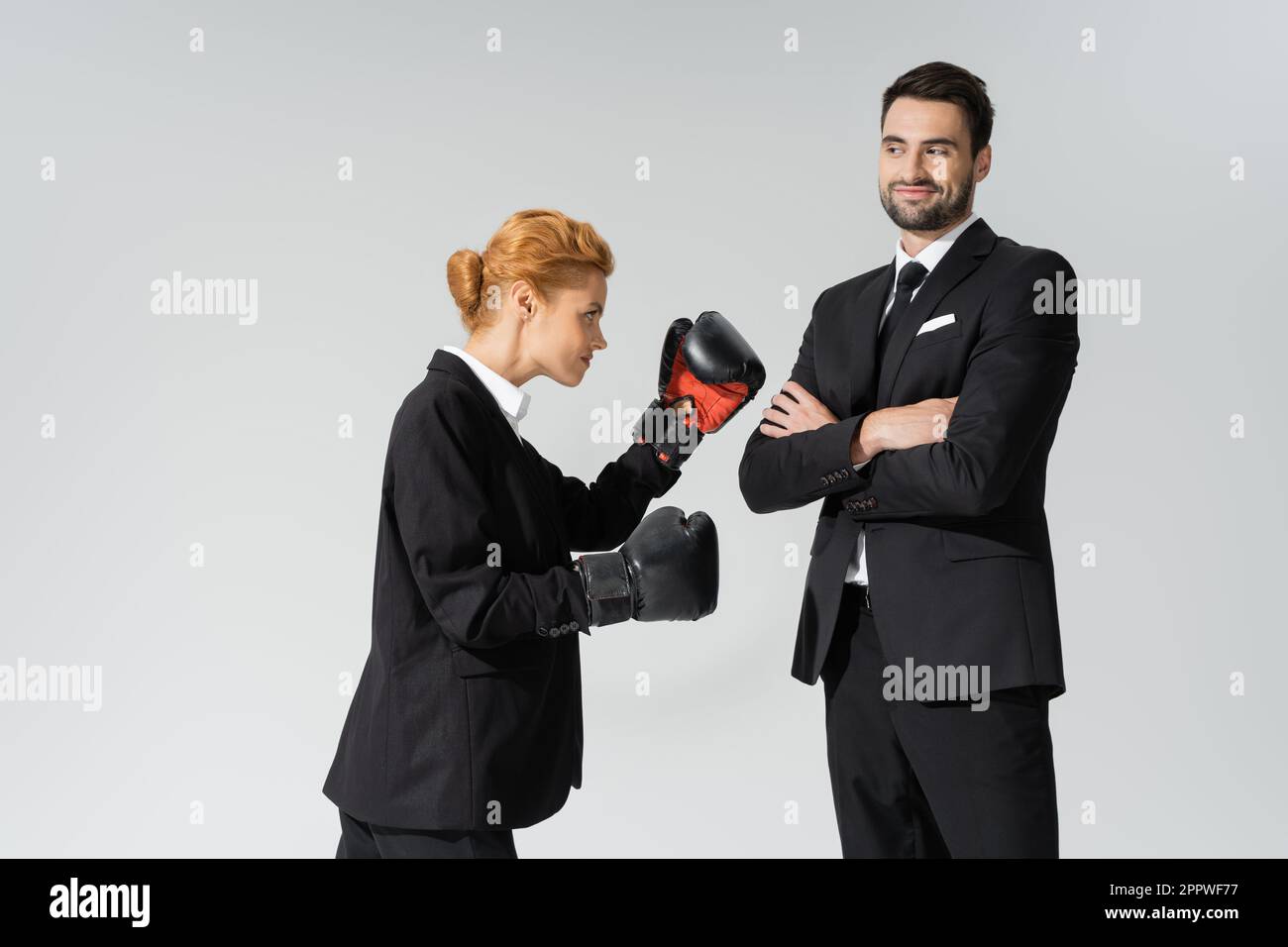 redhead woman in formal wear boxing near cheerful businessman standing ...