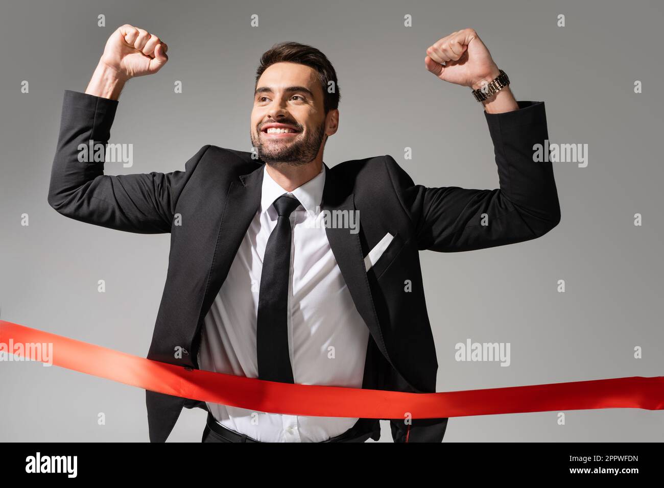 young successful businessman crossing red finish ribbon and showing ...
