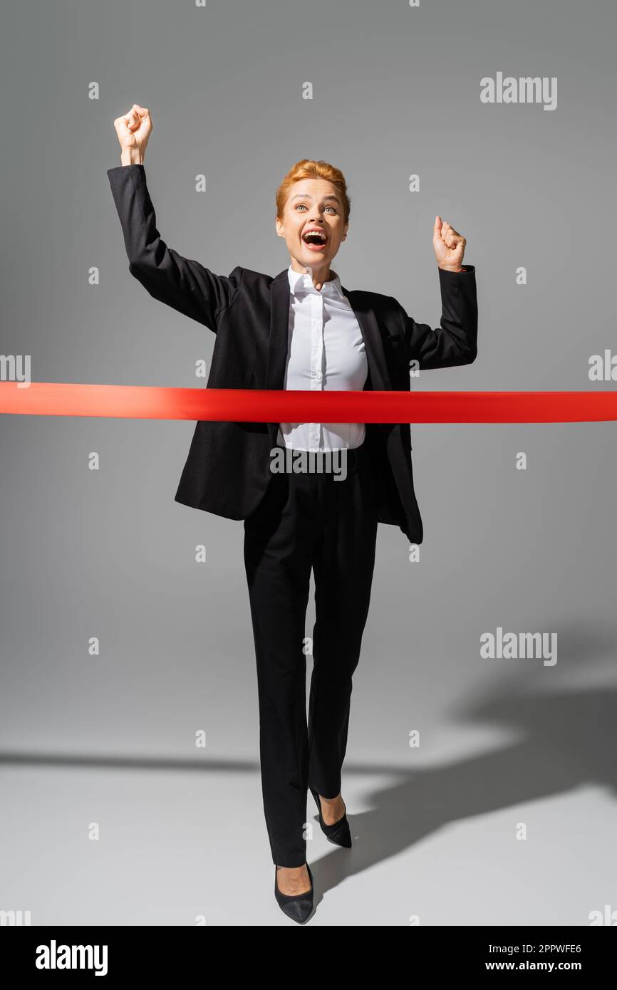full length of overjoyed businesswoman in black suit crossing finish ...