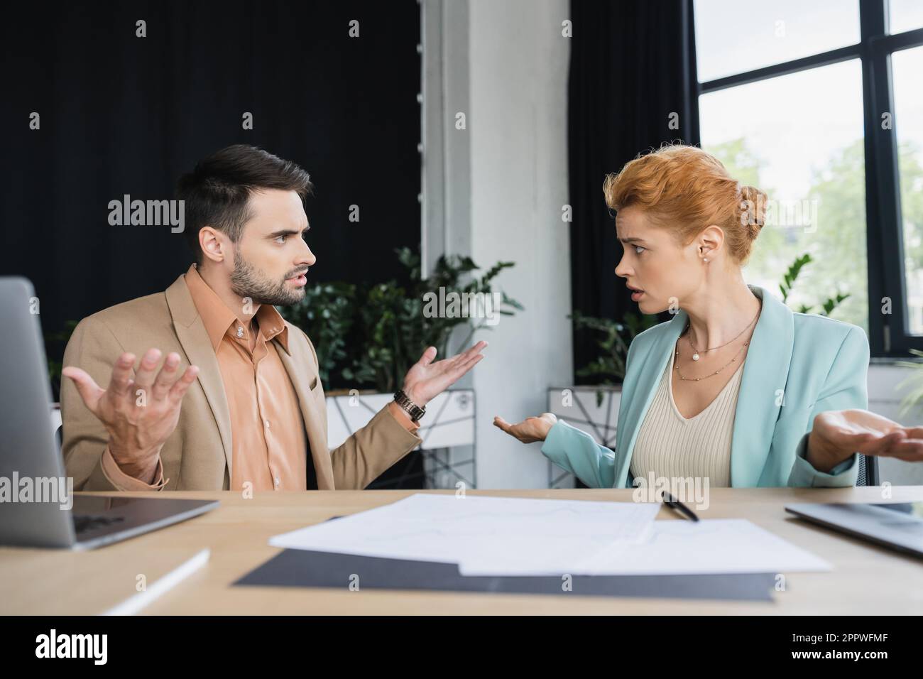 confused managers showing shrug gesture while talking near documents in ...