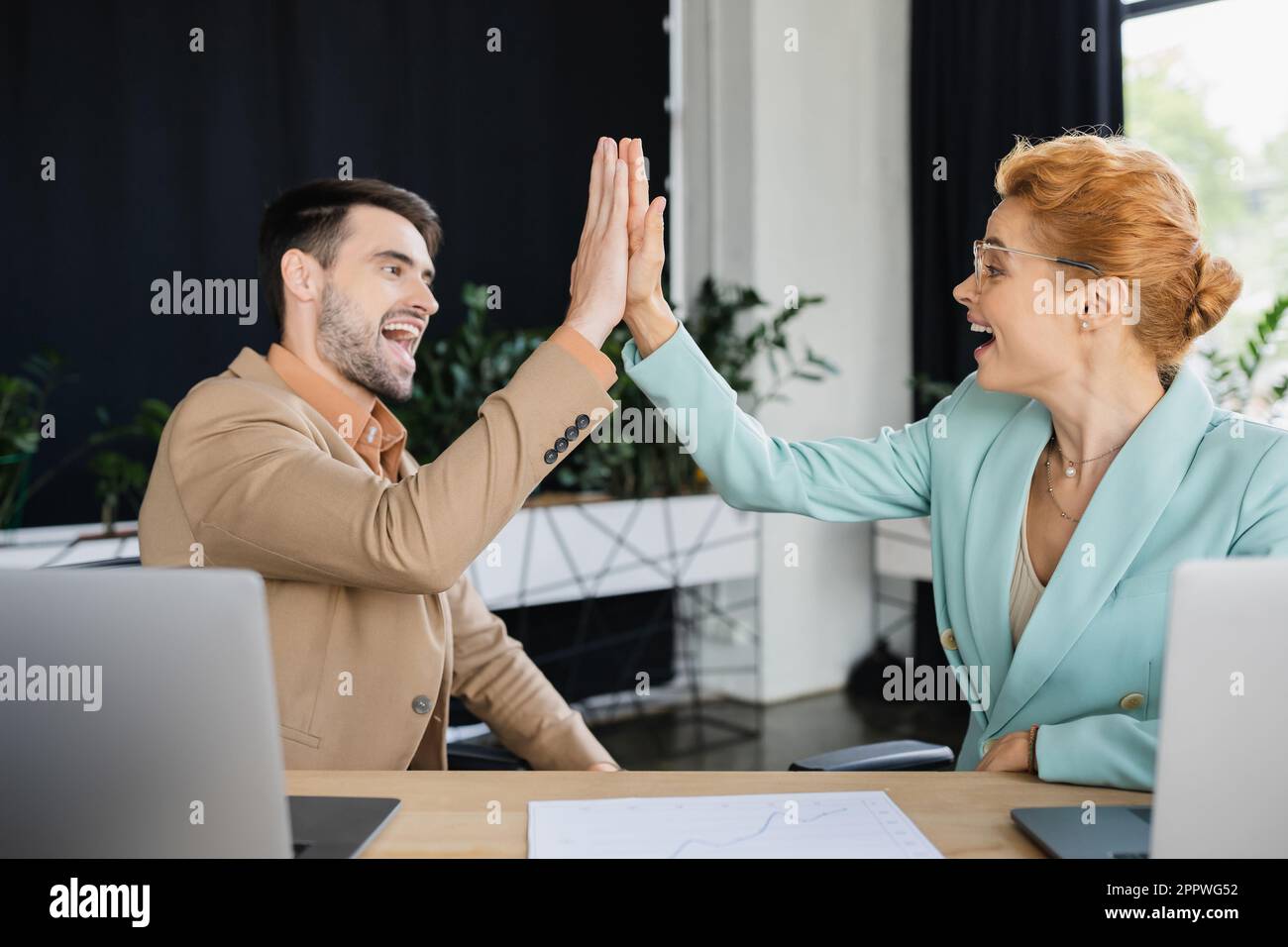 excited and stylish business partners giving high five at workplace in ...
