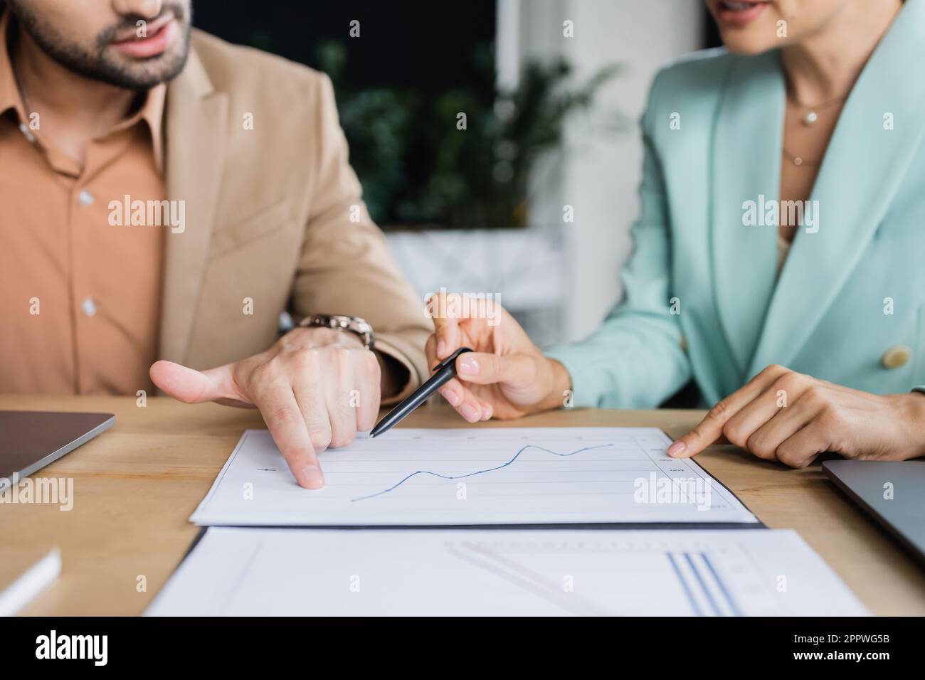 cropped view of business partners pointing at graphs while working with ...