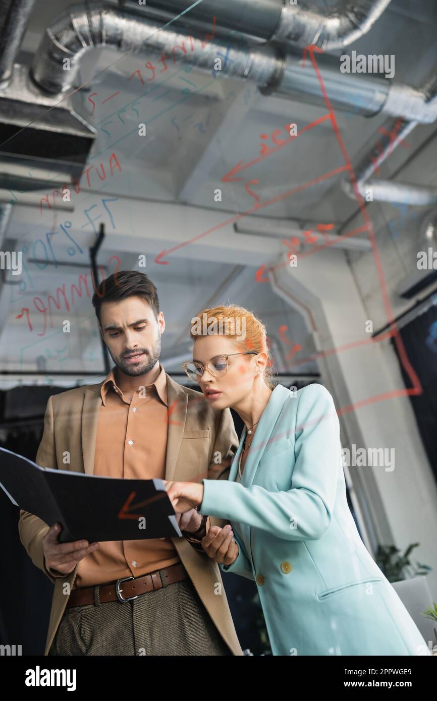 thoughtful business colleagues looking at folder with documents near ...