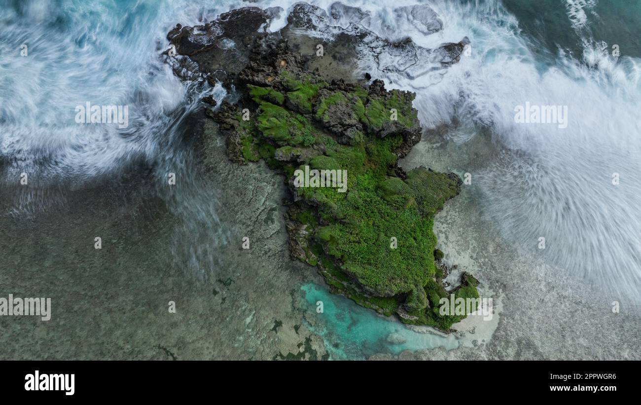 An aerial view of a green island with splashing ocean waves. Arrowhead ...