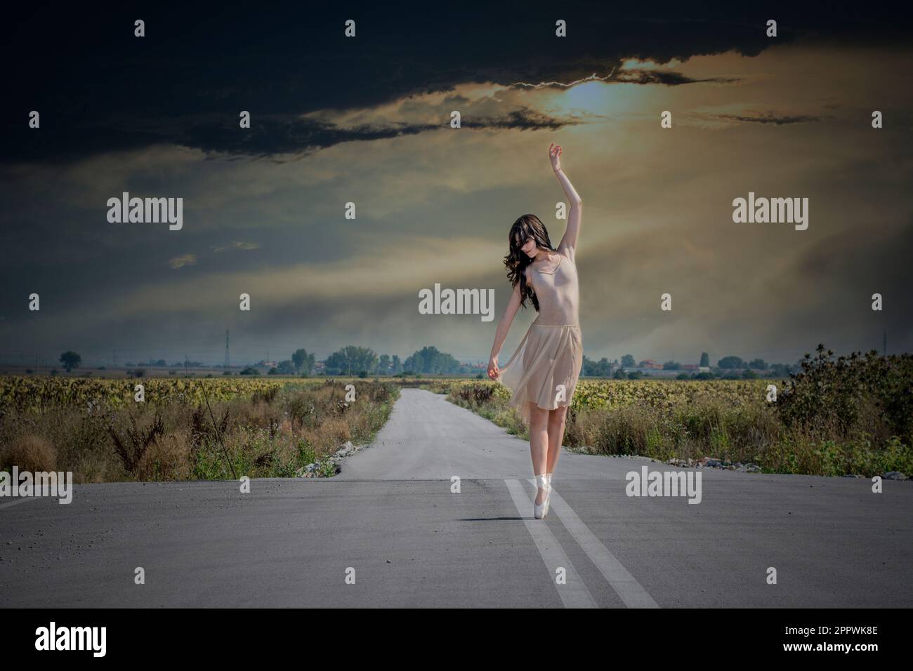 Female ballet dancer dancing in the middle of the road at sunset ...