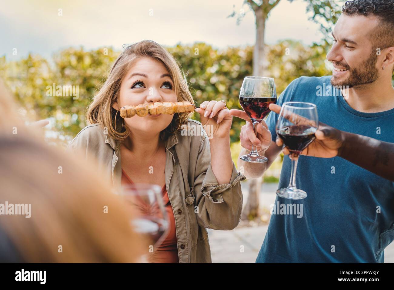 Curvy woman playfully uses a skewer as a mustache at a diverse outdoor ...
