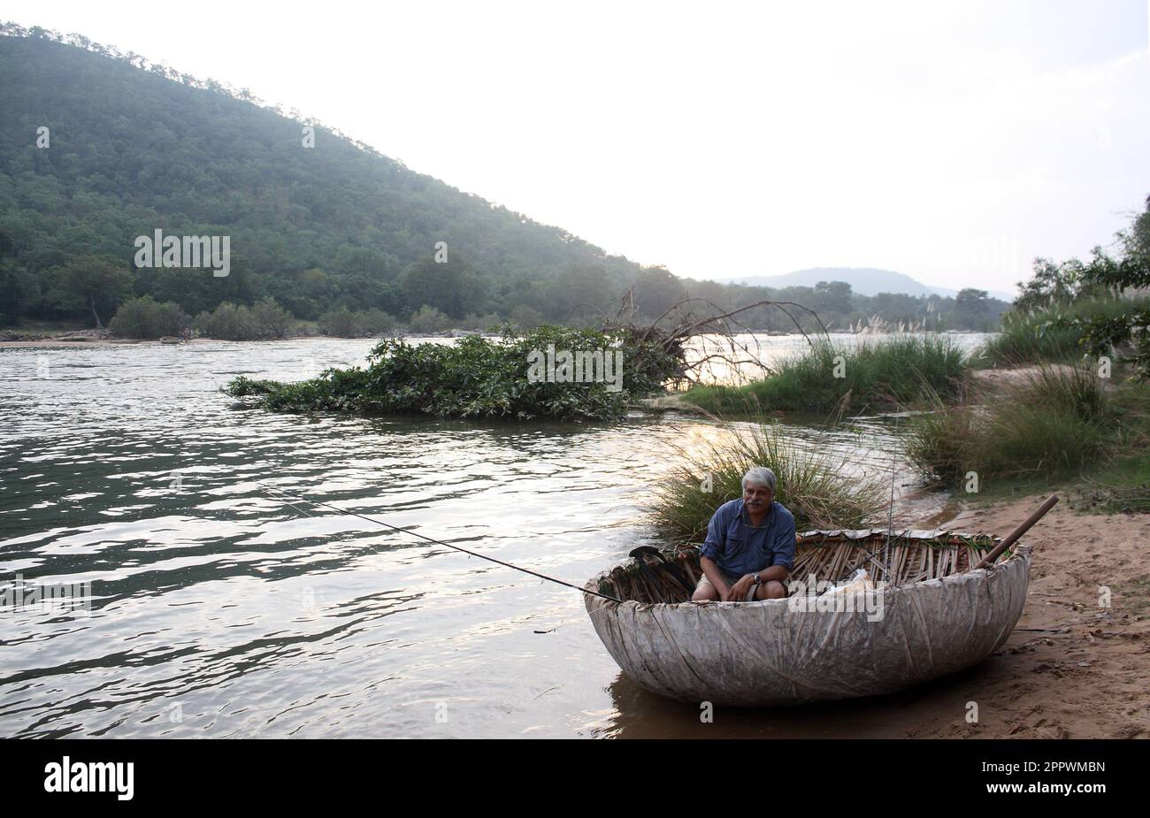 Man sitting in a traditional coracle boat on a riverbank by Cauvery ...