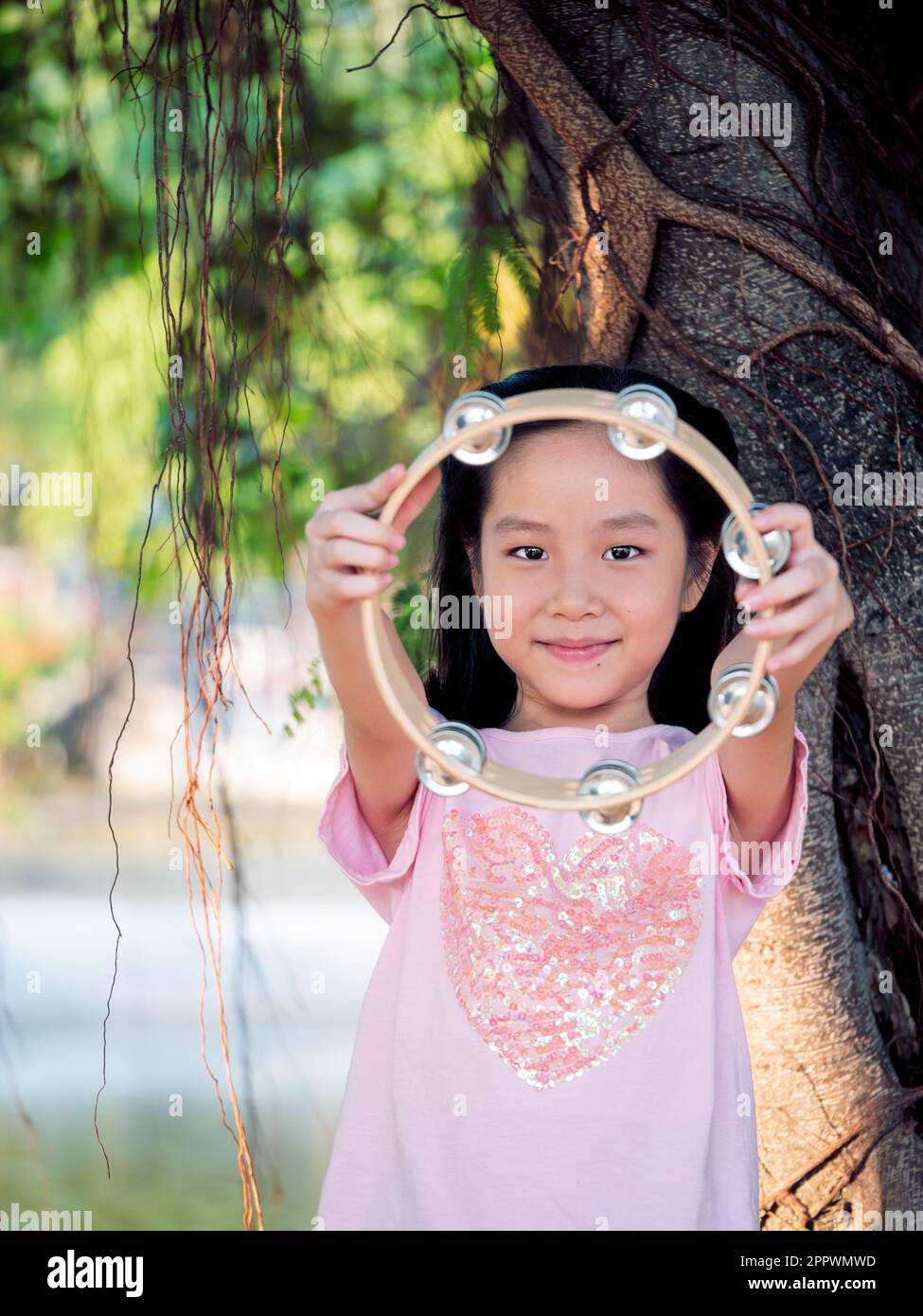 Little asian child girl play the tambourine, in the garden under the ...