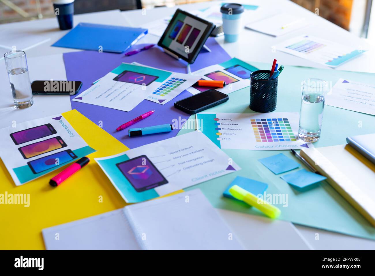 Tablet, smartphones and mock up visuals on busy table top at design ...