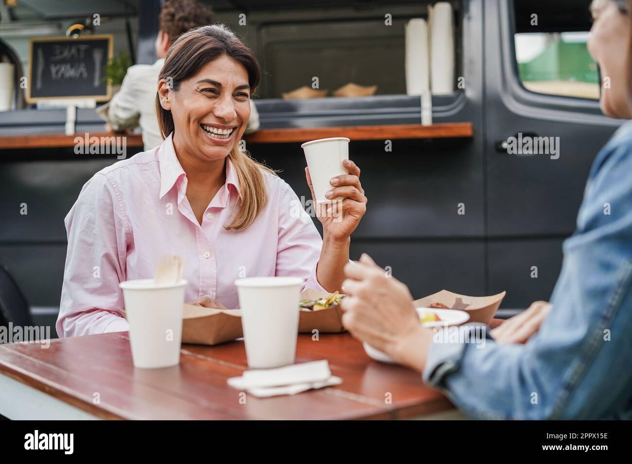 Mature friends having fun eating and drinking outdoor at food truck ...