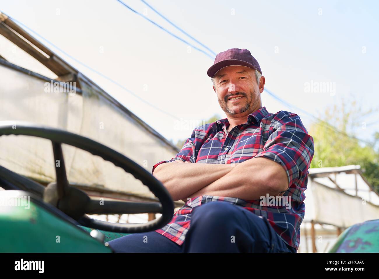 Portrait of smiling mature male farmer sitting with arms crossed on ...