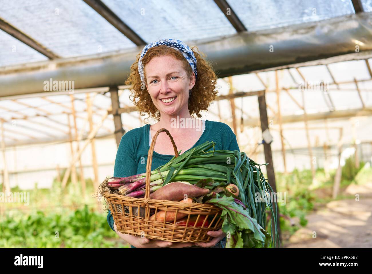 Portrait of female farmer with curly hair holding organic vegetables ...