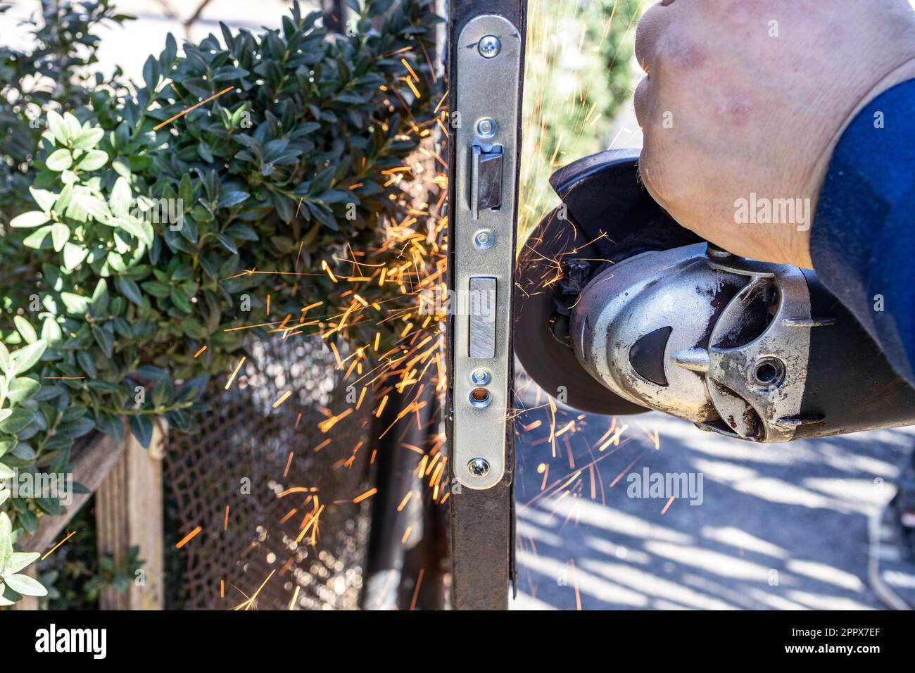 worker installs door lock in iron wicket using electric grinder close ...